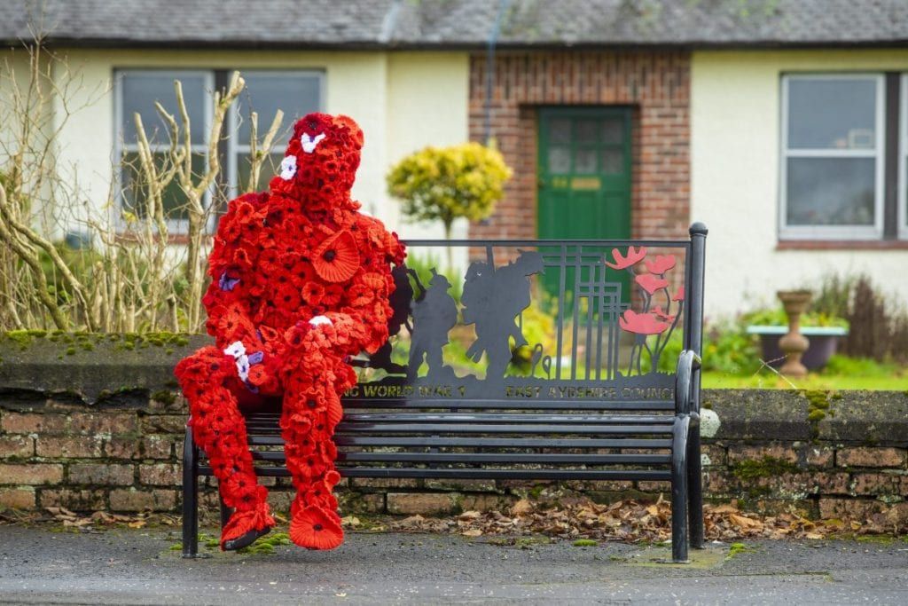 Human figure "Poppy Man" made from crocheted poppies sitting on a ...